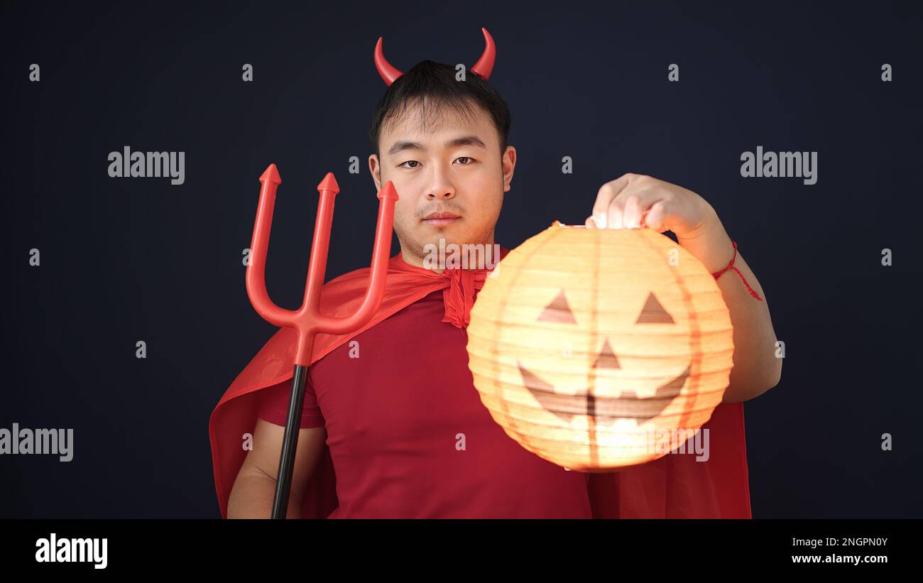 Young chinese man wearing devil costume holding pumpkin lamp over ...