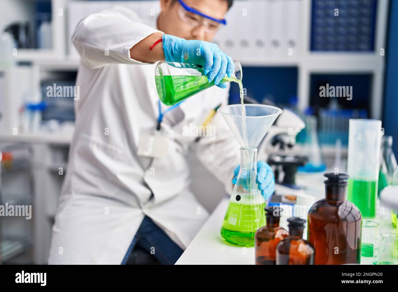 Young chinese man wearing scientist uniform measuring liquid at ...
