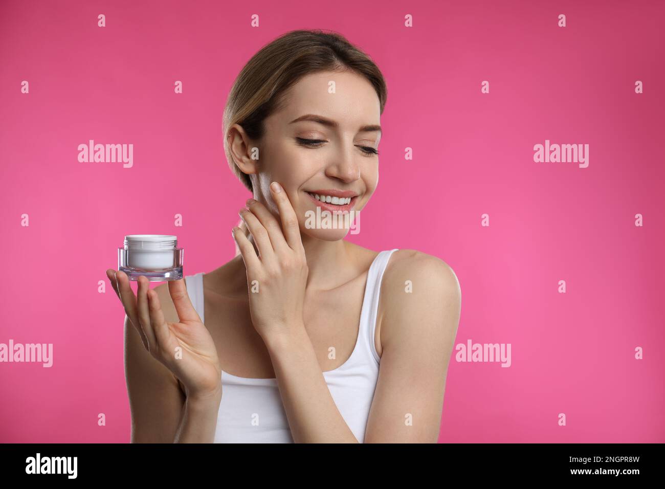 Young woman applying facial cream on pink background Stock Photo - Alamy