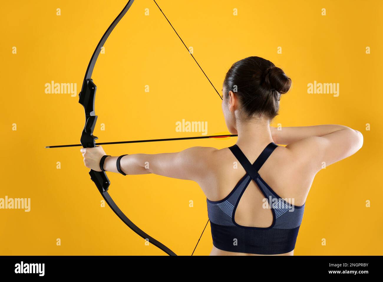 Woman with bow and arrow practicing archery on yellow background, back ...