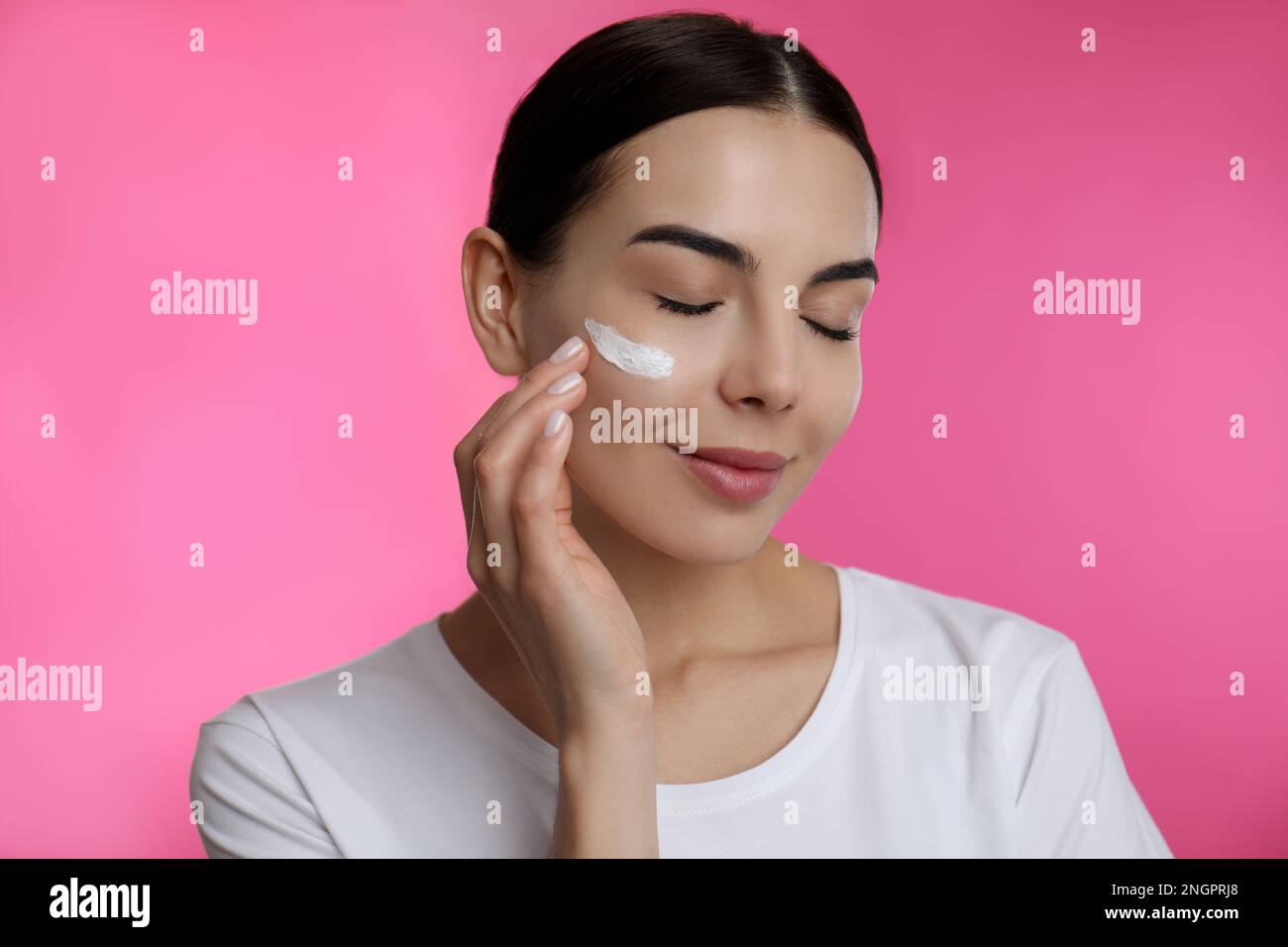 Young woman applying facial cream on pink background Stock Photo - Alamy