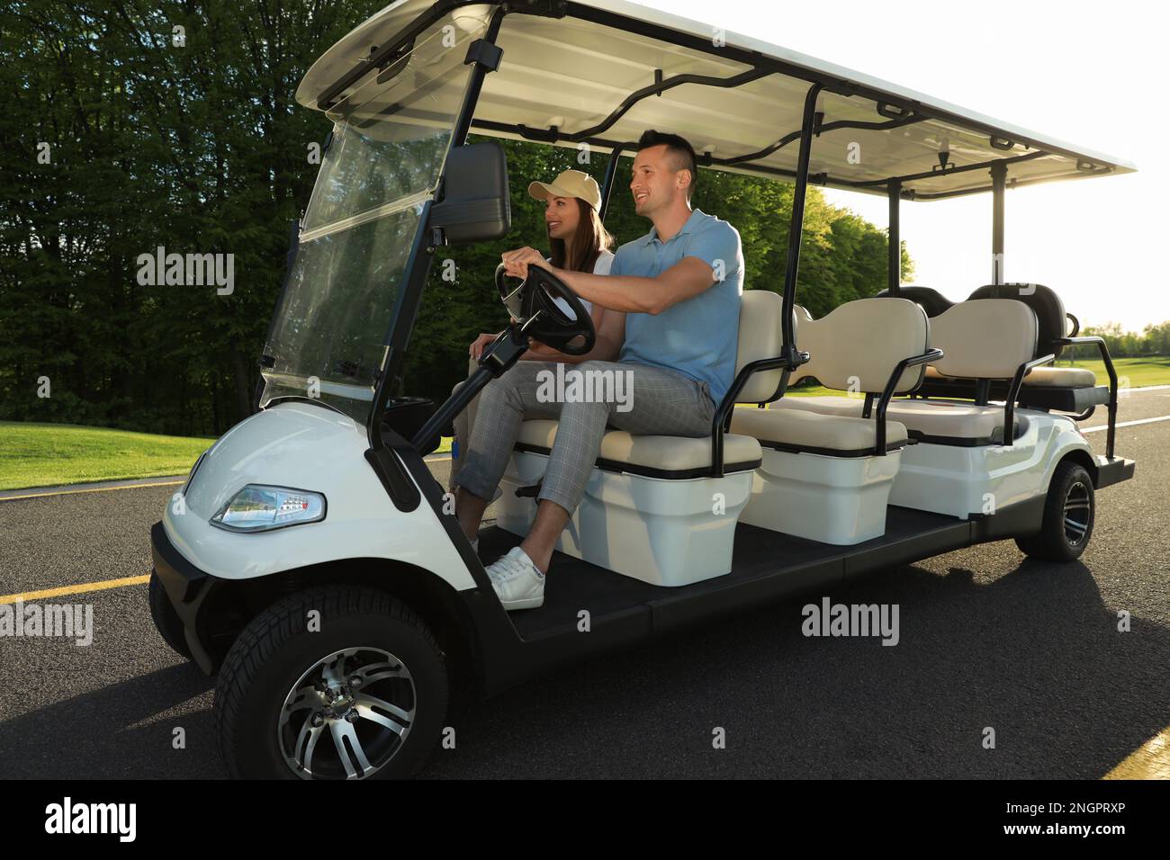 Happy couple driving golf cart on road in park Stock Photo - Alamy