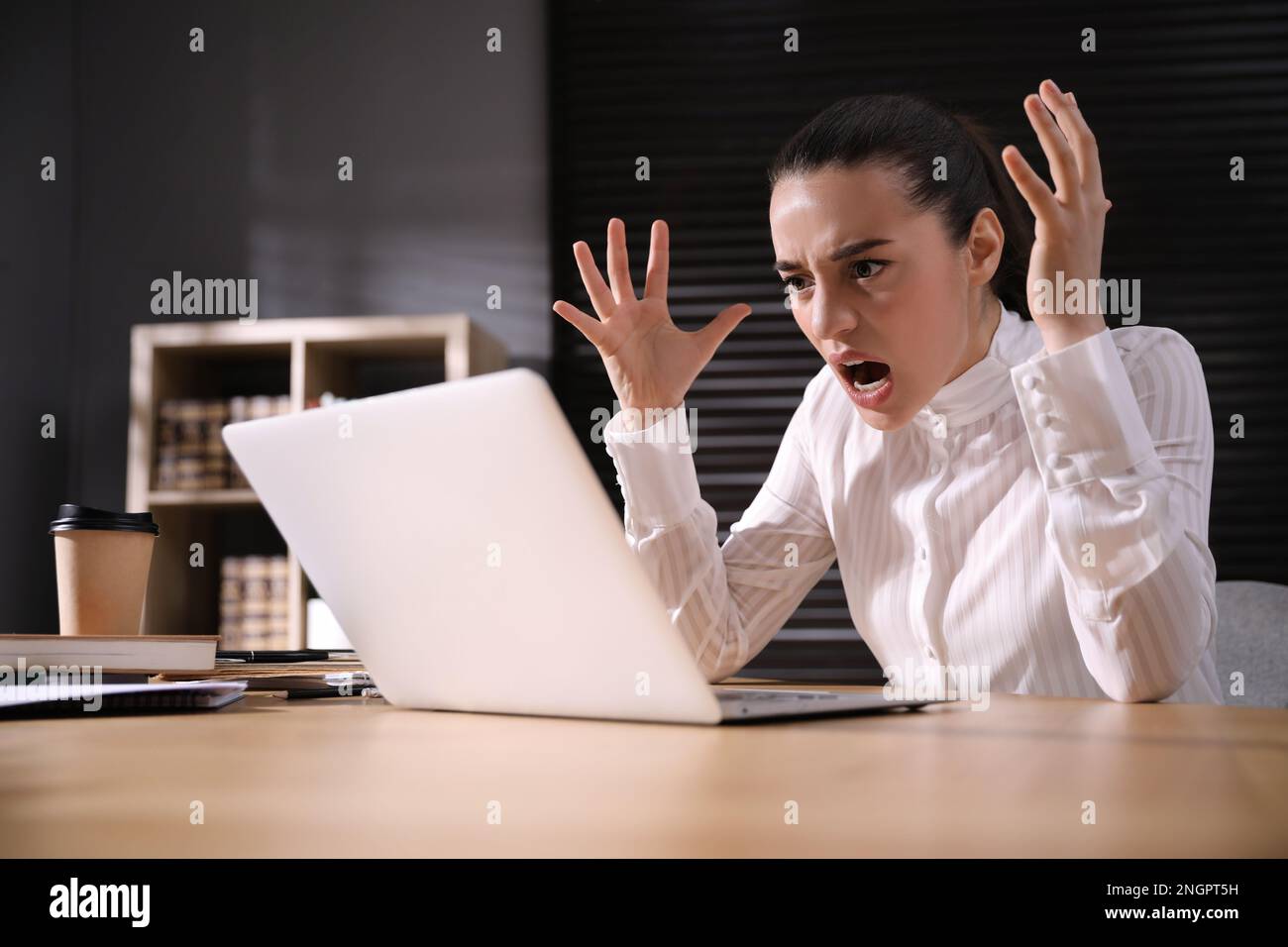 Emotional young businesswoman working on laptop in office. Online hate ...