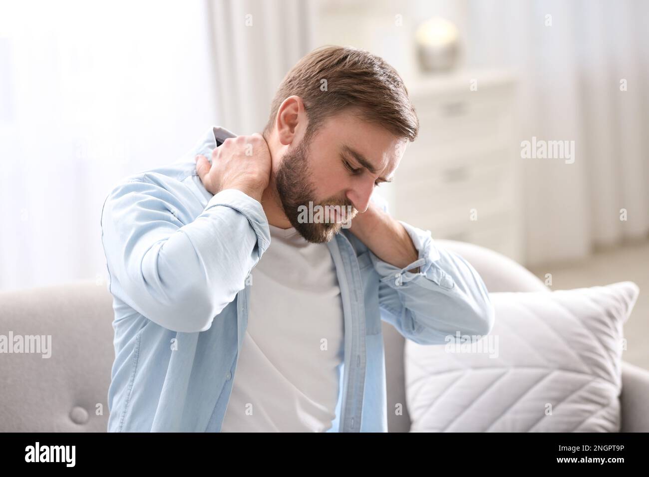 Man suffering from neck pain at home. Bad posture problem Stock Photo ...