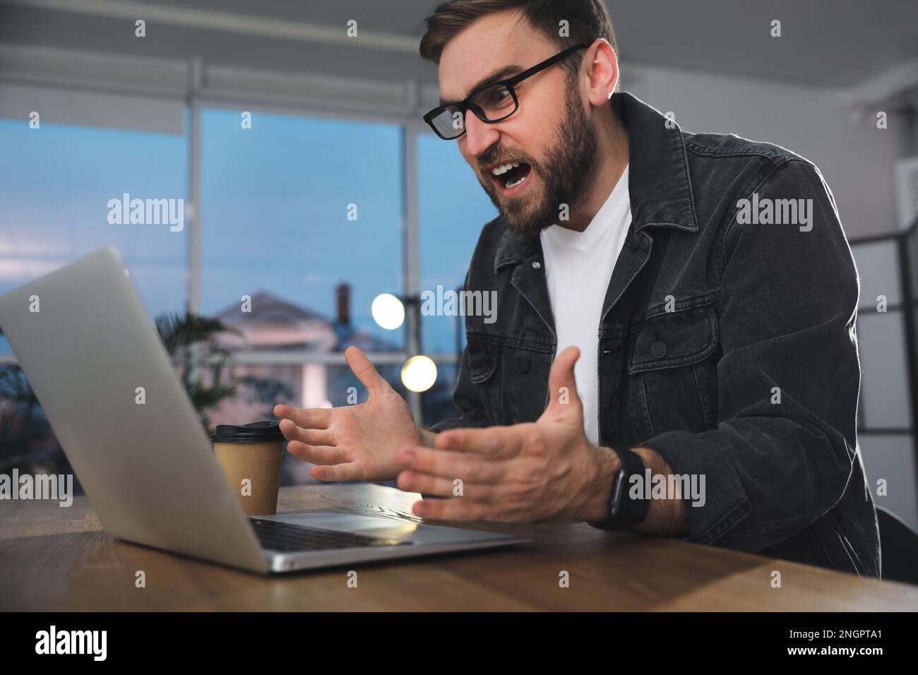Emotional young man working on laptop in office. Online hate concept ...