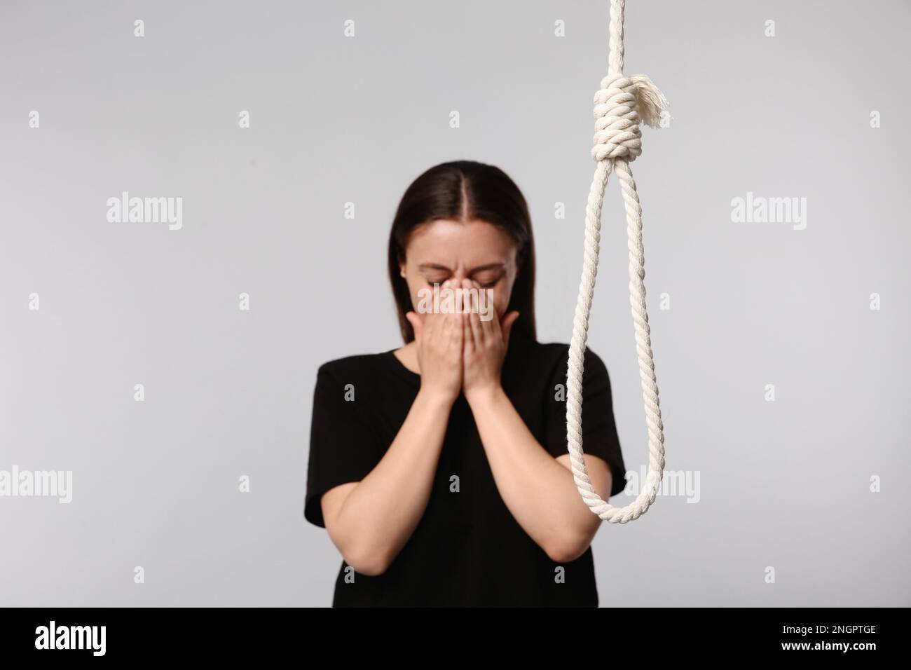 Depressed woman crying near rope noose on light grey background Stock ...