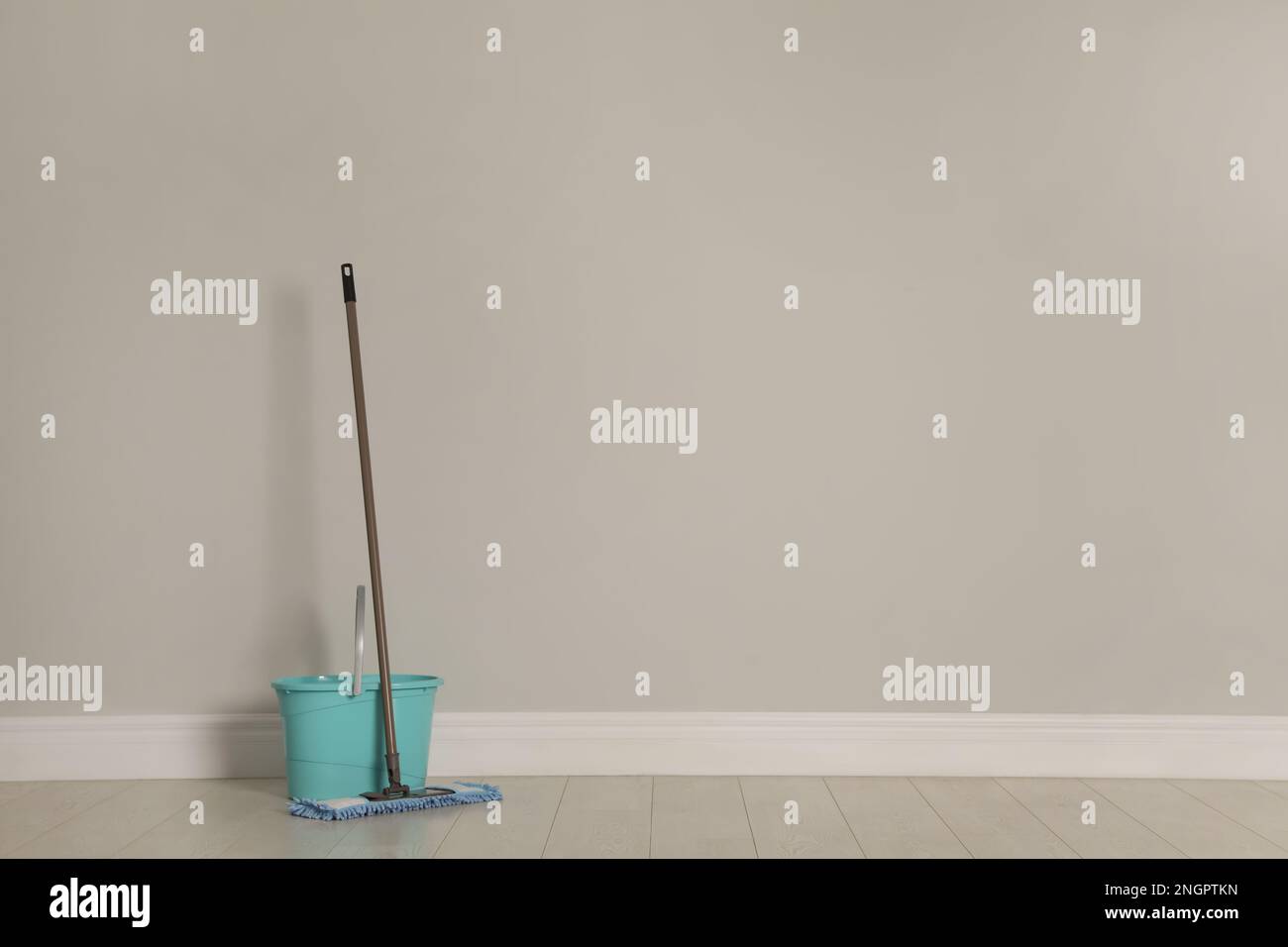 Mop and bucket on wooden floor near light grey wall, space for text ...