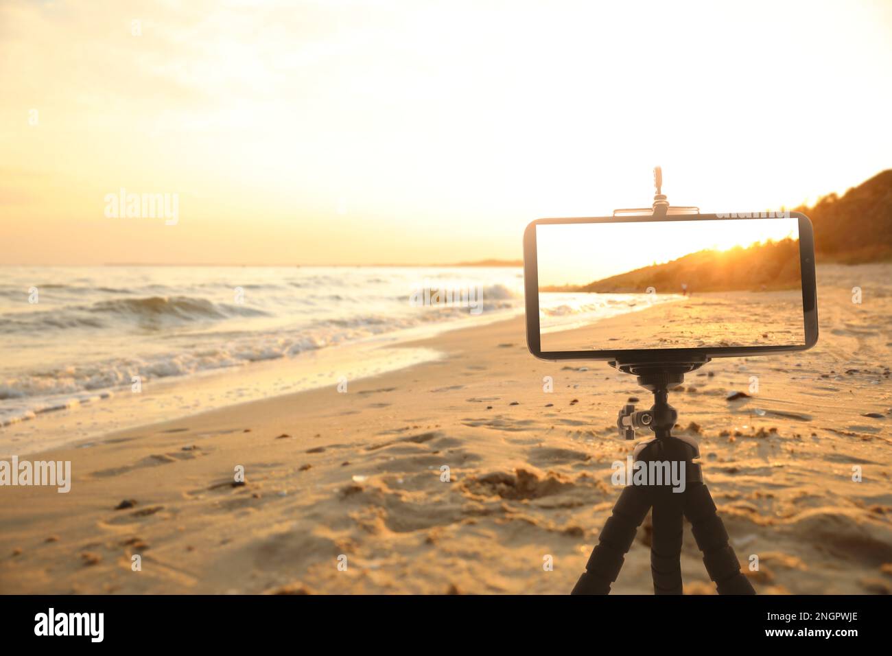 Taking photo of beautiful sandy beach with smartphone mounted on tripod ...