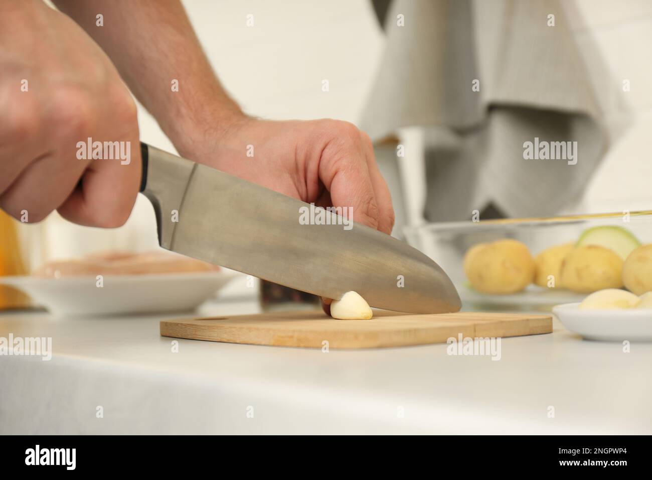 Man cutting garlic at table in kitchen, closeup Stock Photo - Alamy