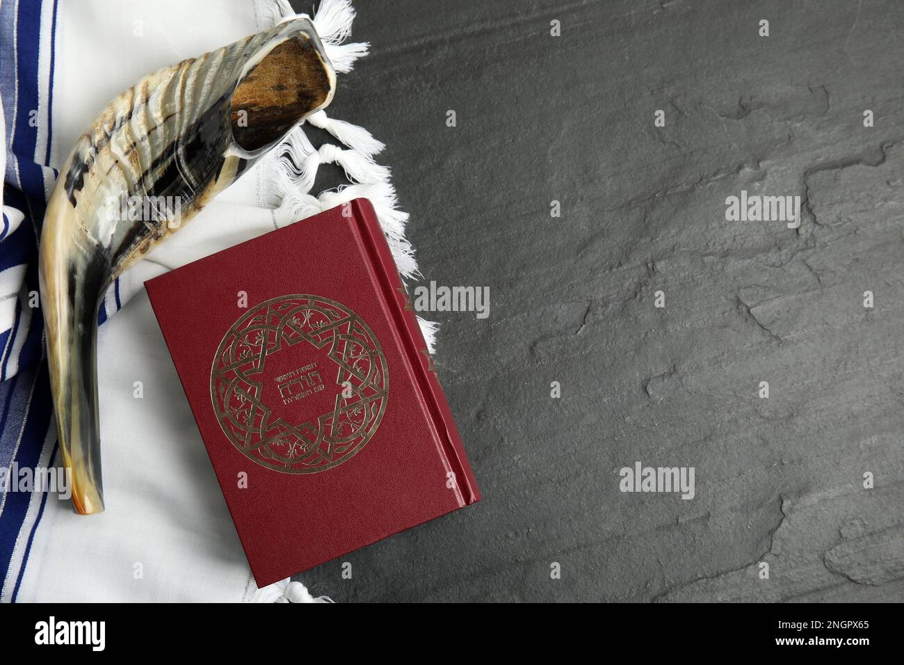 Tallit, shofar and book Torah with text in Hebrew on black slate table ...