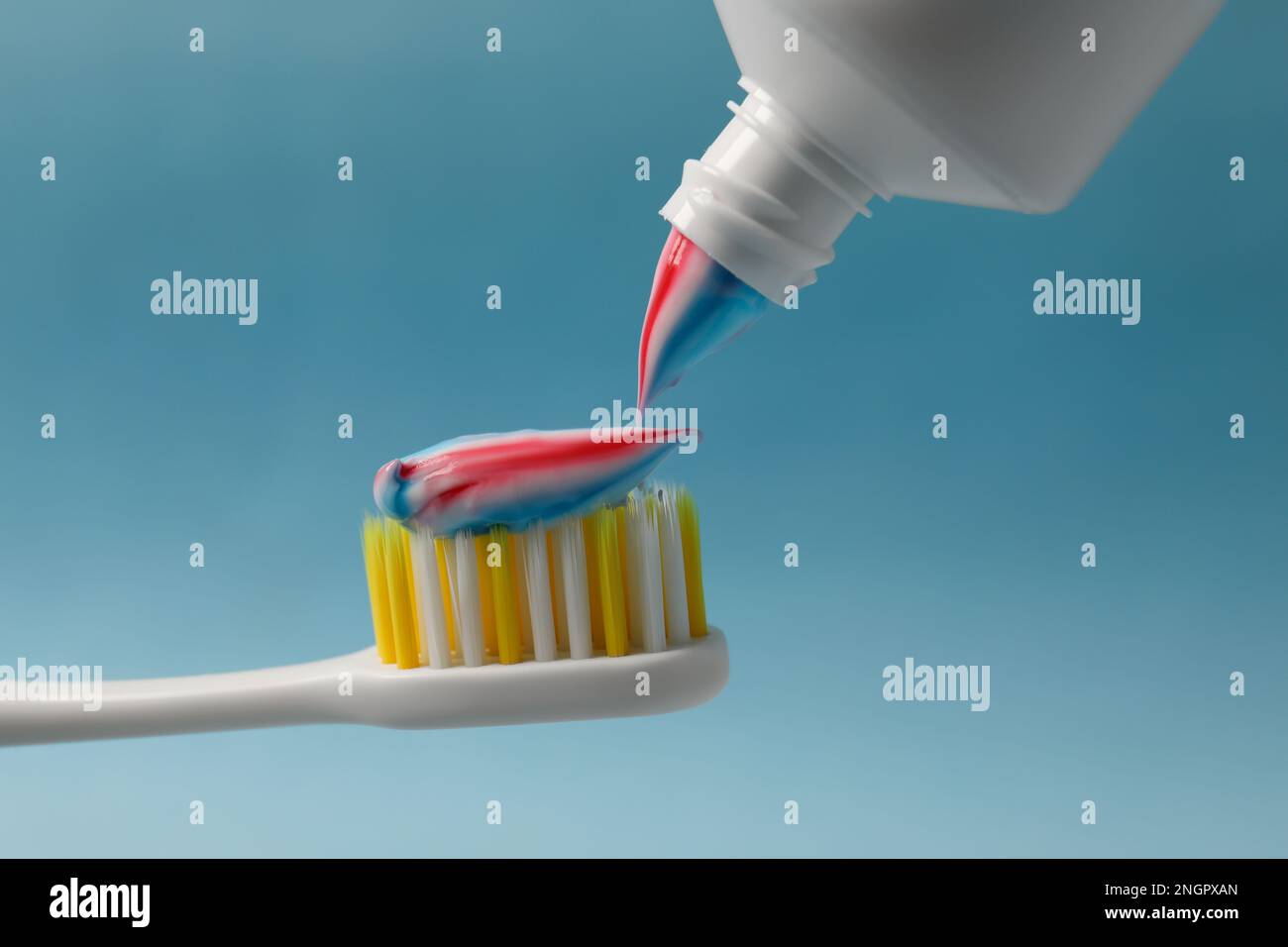 Squeezing toothpaste onto brush against light blue background, closeup ...