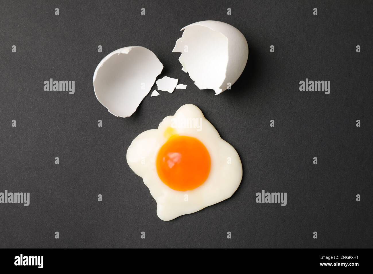 Sweet gummy fried egg and broken shell of real one on black background ...