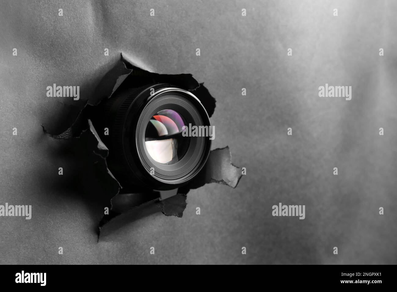 Hidden camera spying through torn hole in black paper, space for text ...