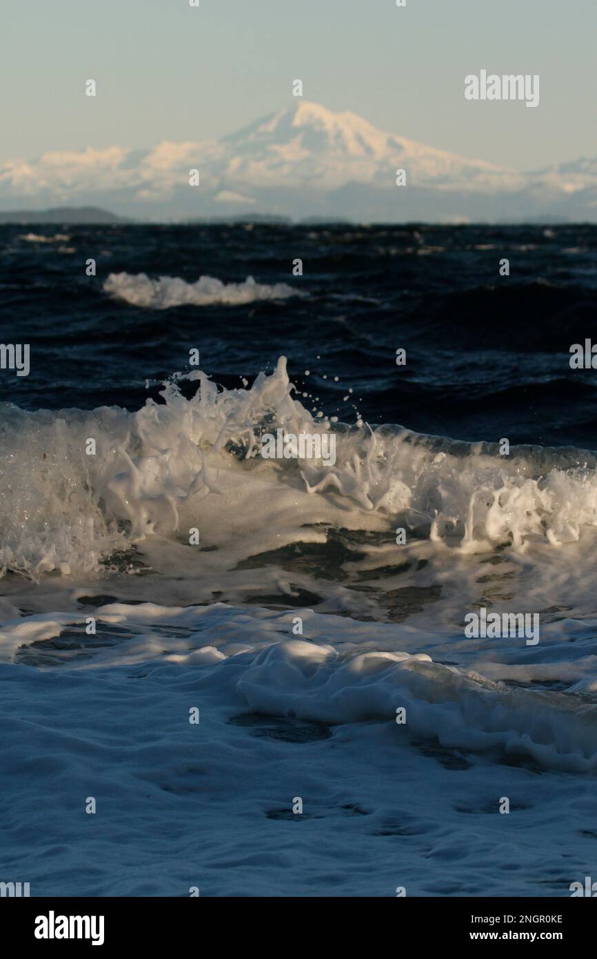 A wave crashing in the foreground of the Pacific Ocean, with Mount ...