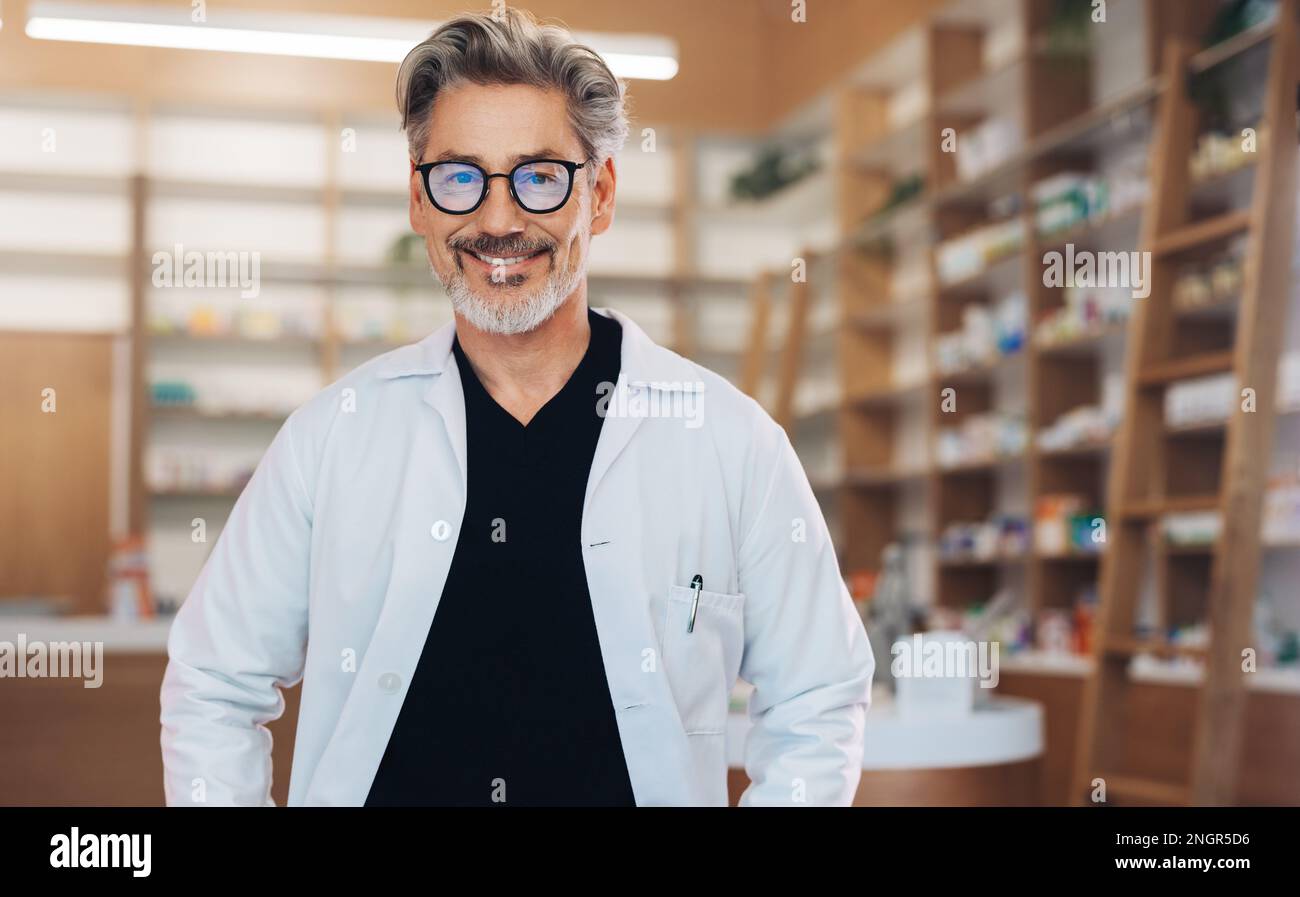 Portrait of a male pharmacist standing in a drug store in a white lab ...