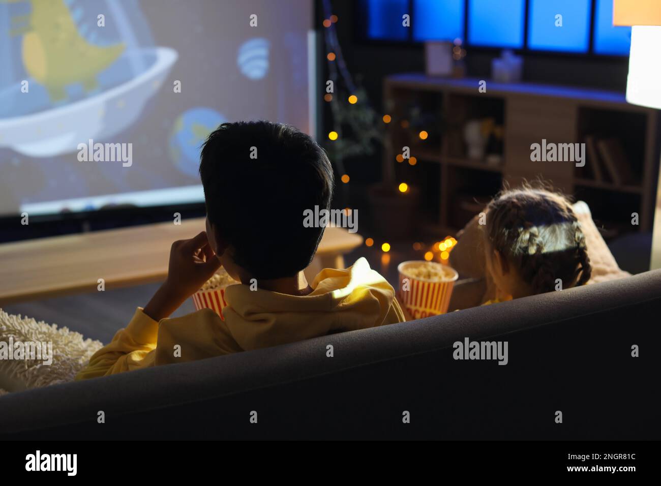 Little boy and his sister with popcorn watching cartoons on projector ...