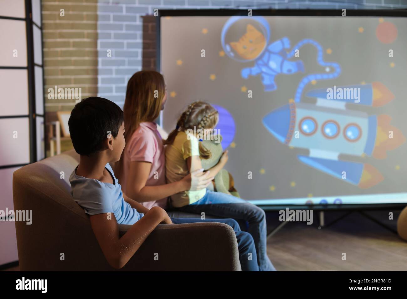 Little boy with his mother and sister watching cartoons on projector ...