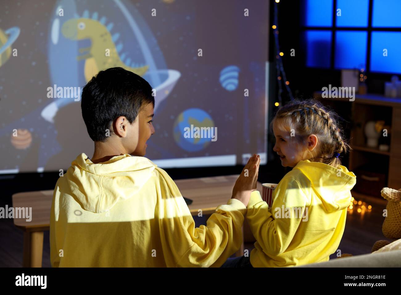 Little boy and his sister watching cartoons on projector screen at home ...