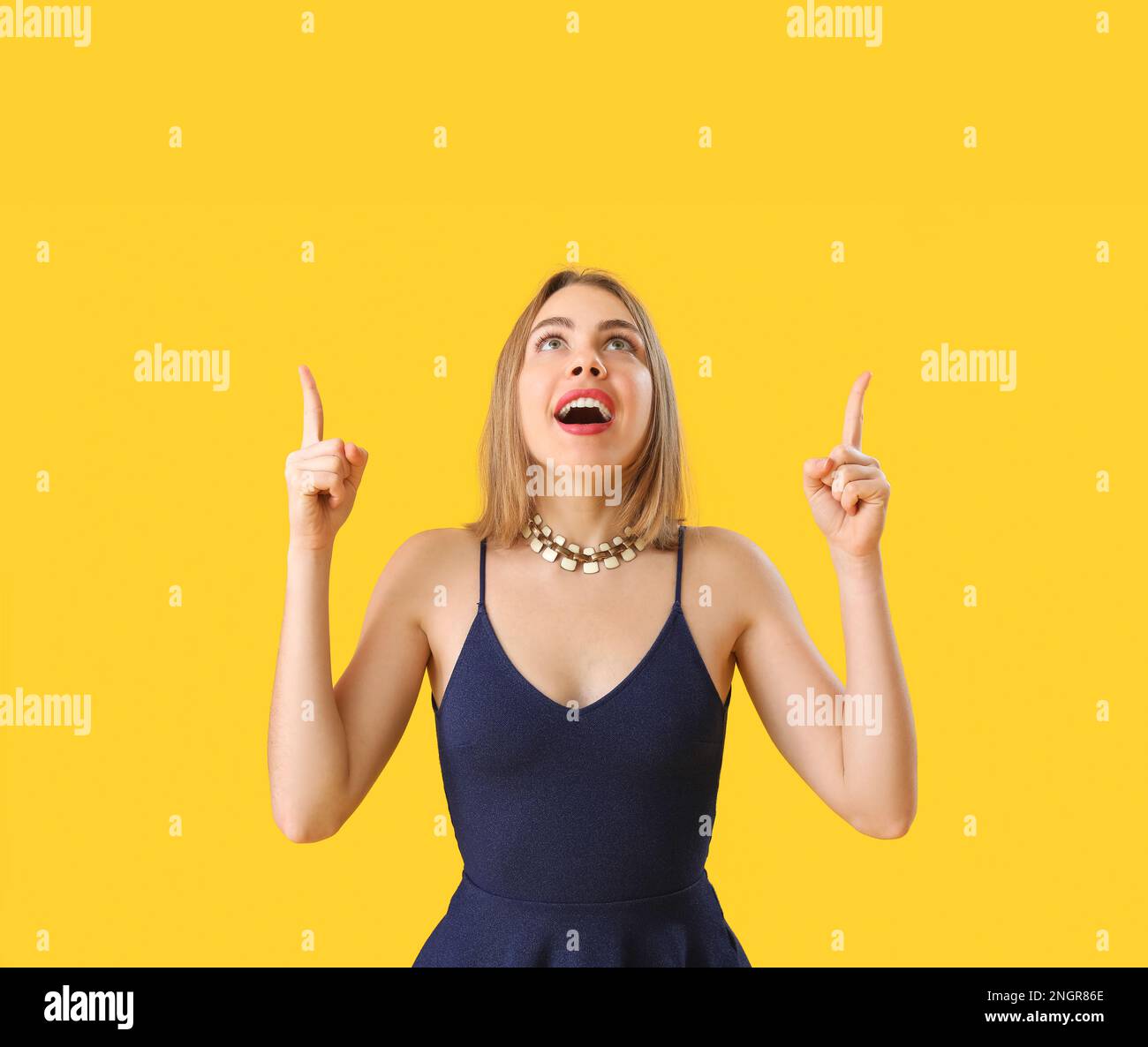 Young woman with necklace pointing at something on yellow background ...
