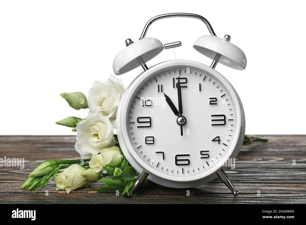 Alarm clock and beautiful eustoma flowers on wooden table against white ...