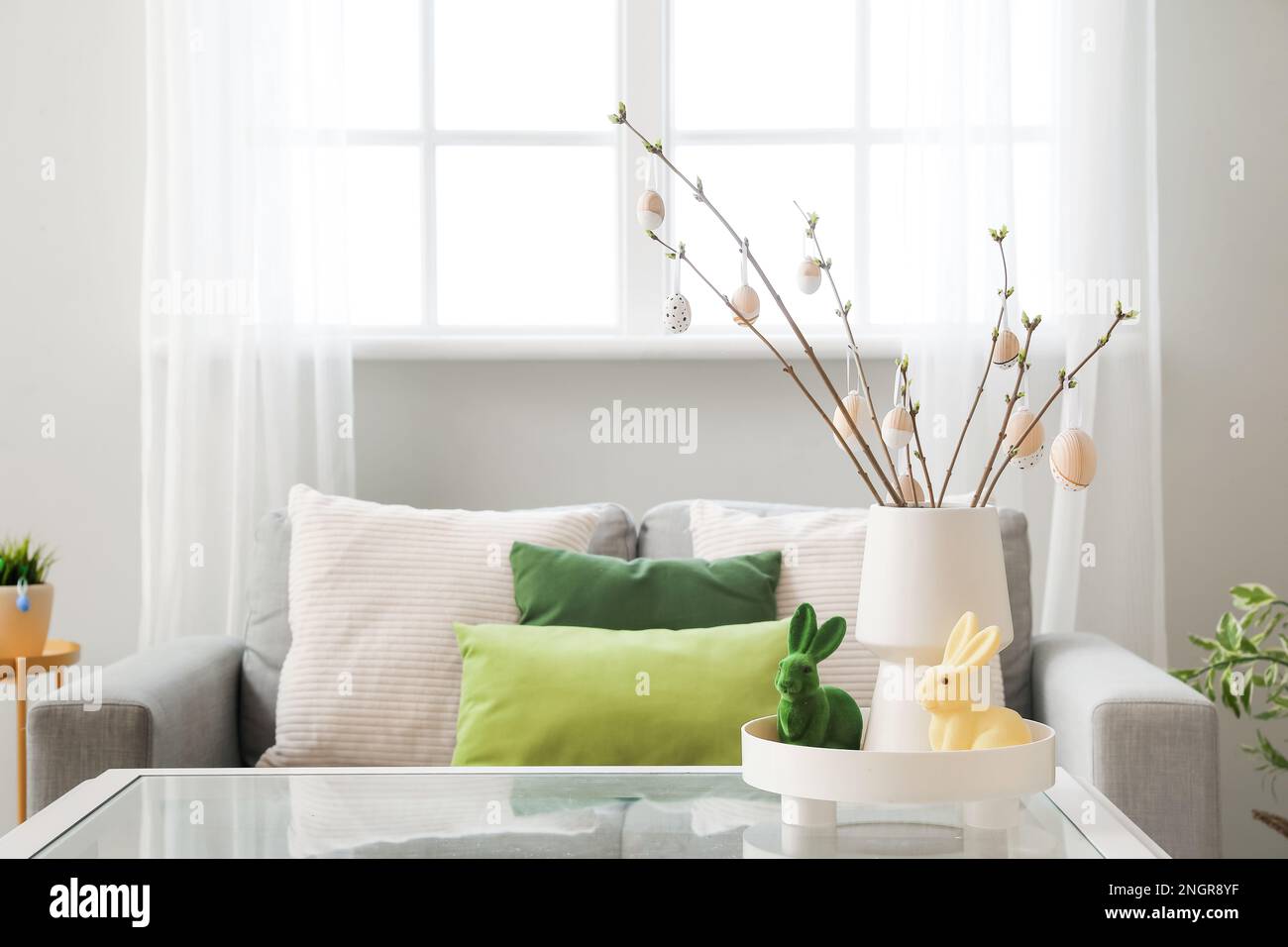 Vase with tree branches, Easter eggs and rabbits on table in light ...