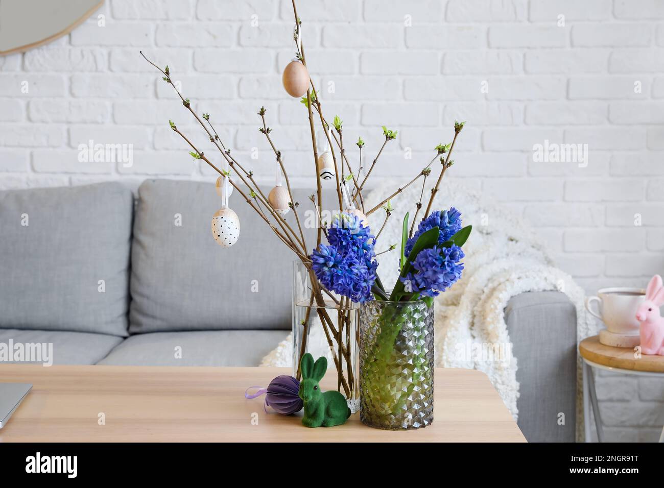 Vases with flowers, tree branches, Easter eggs and rabbit on table in ...