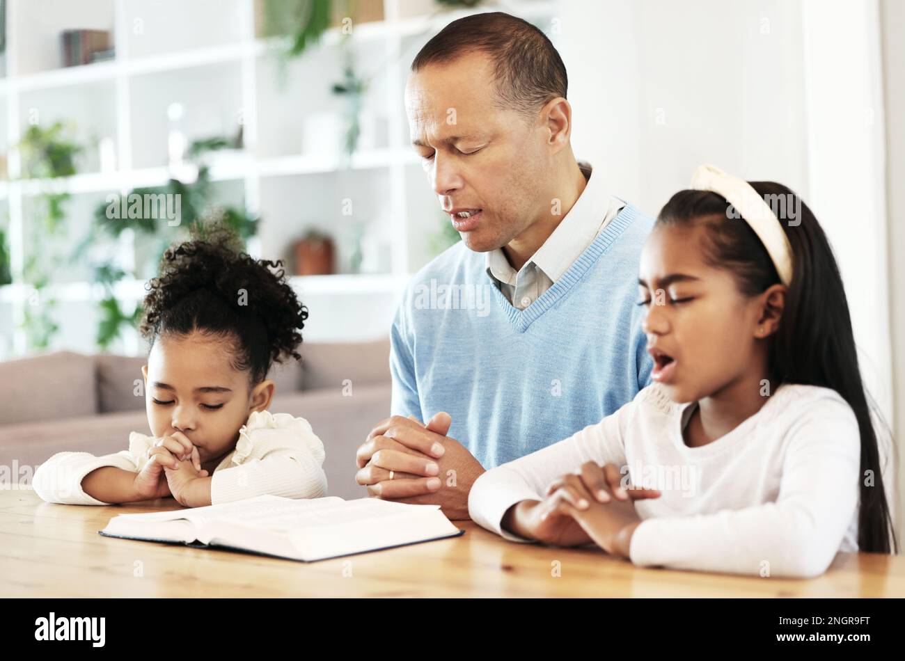 Family, worship and bible with father and kids praying at table for ...