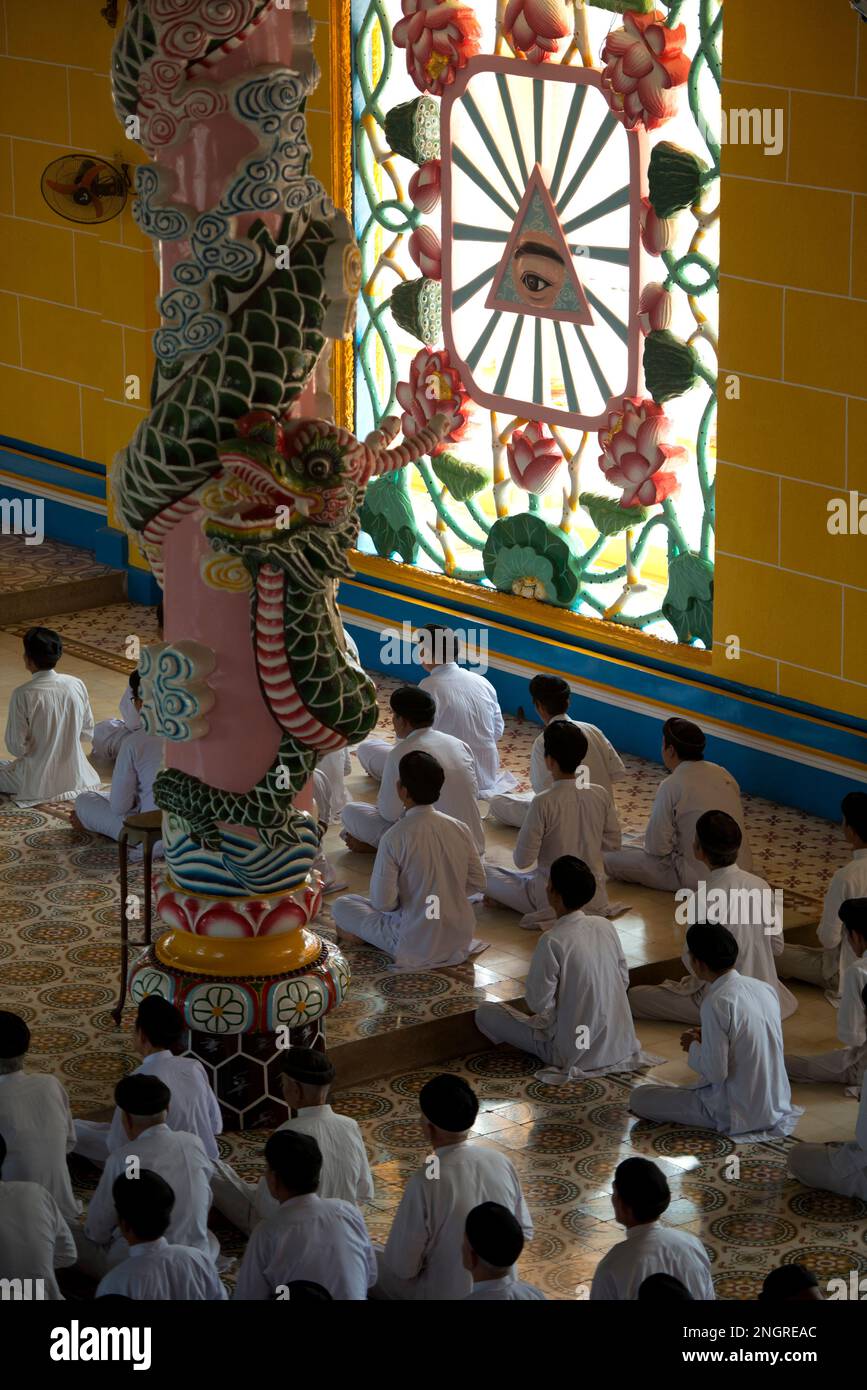 Male Caodaist disciples, sitting during ceremony by colorful columns ...