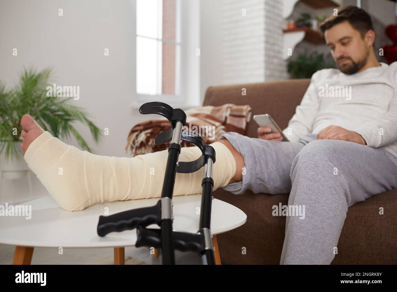 Man sitting on the sofa with his broken leg resting on a foot stool ...