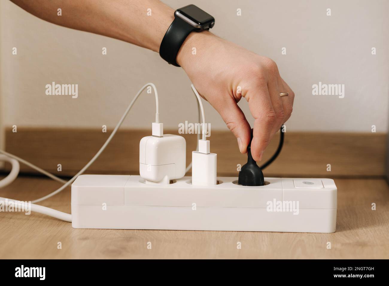 Human hand puts the charger into a filled extension cord. White cable ...