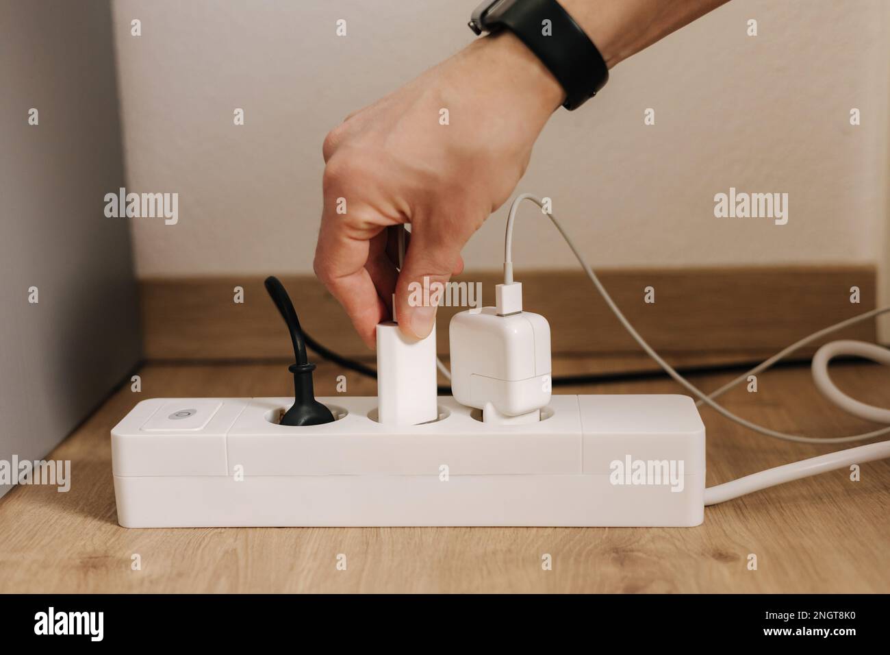 Human hand puts the charger into a filled extension cord. White cable ...