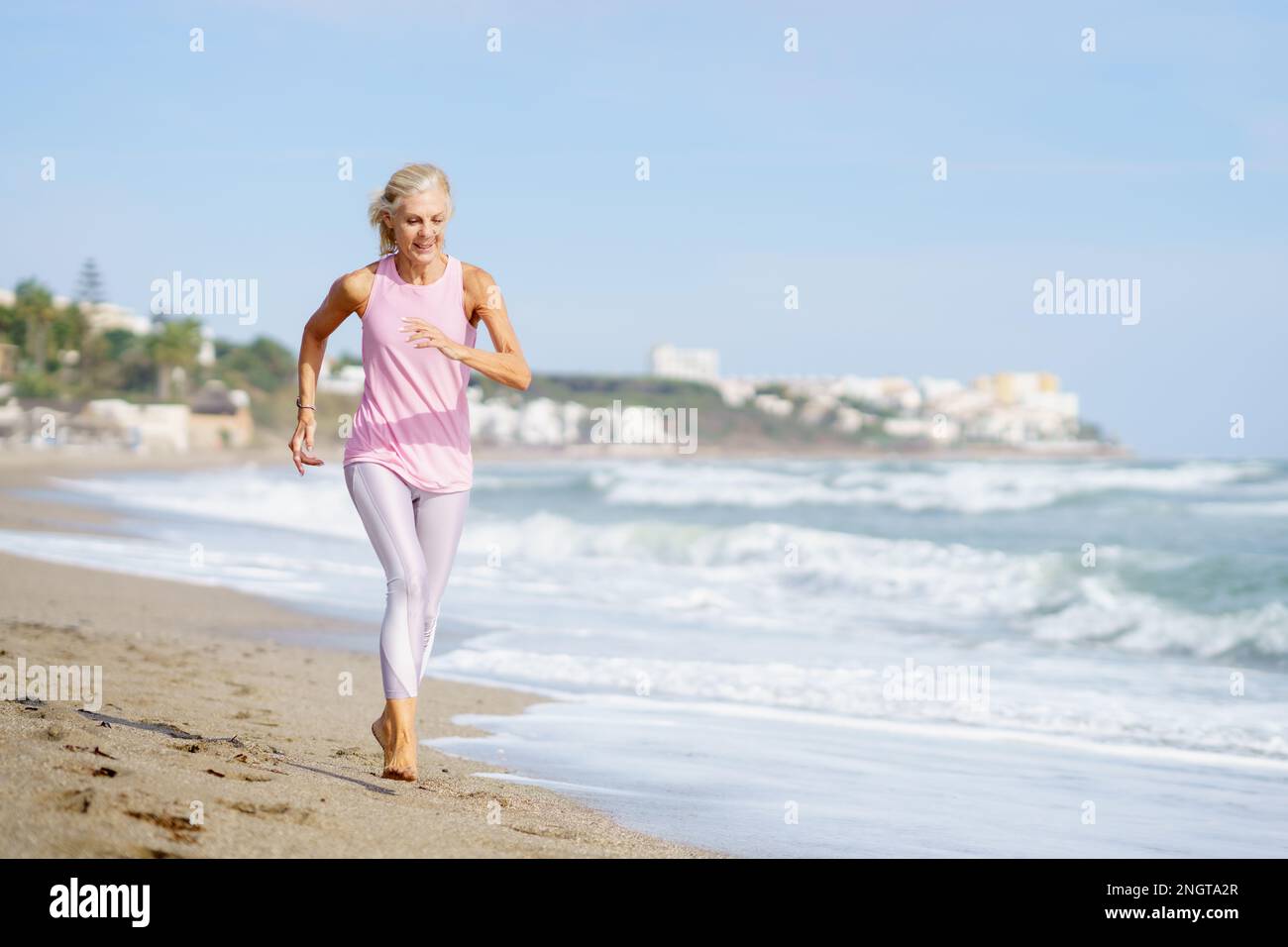 Older female doing sport to keep fit. Mature woman running along the shore of the beach Stock ...