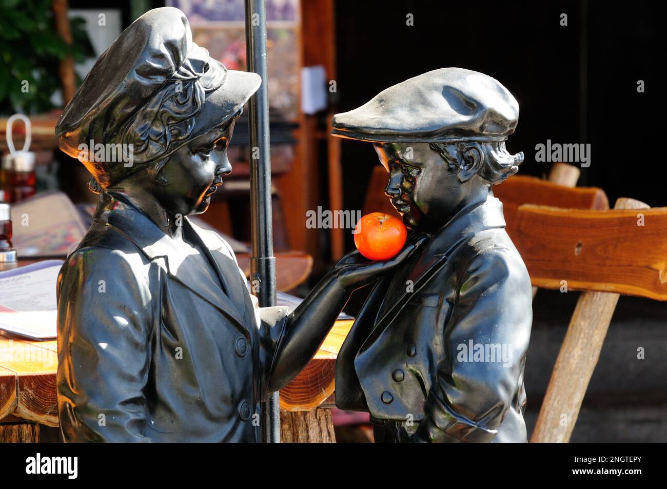 Statues of different gender in front of a restaurant holding a tomato ...