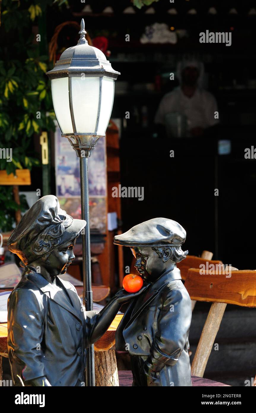 Statues of different gender in front of a restaurant holding a tomato ...