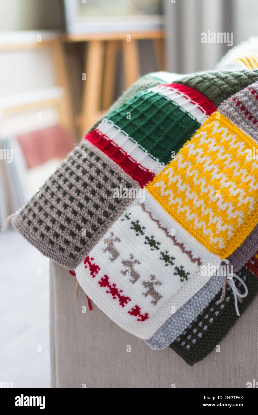 Knitted warm blanket on bed. Woolen plaid on white sofa. Patchwork ...