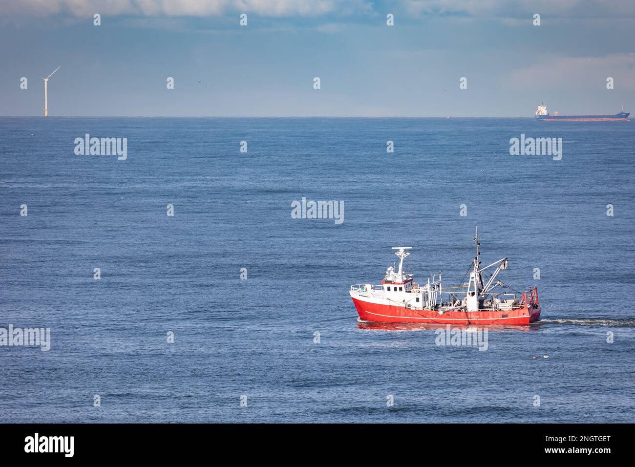 A red cutter on the North sea with a cargo ship and a wind turbine in ...