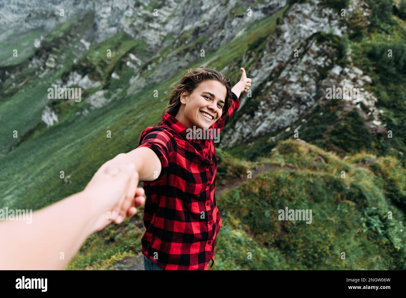 A young happy woman holds the hand of a partner in the mountains ...