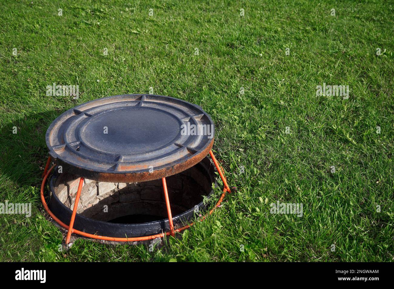 Open well hatch on green lawn. Manhole cover is on stand. Device for ...