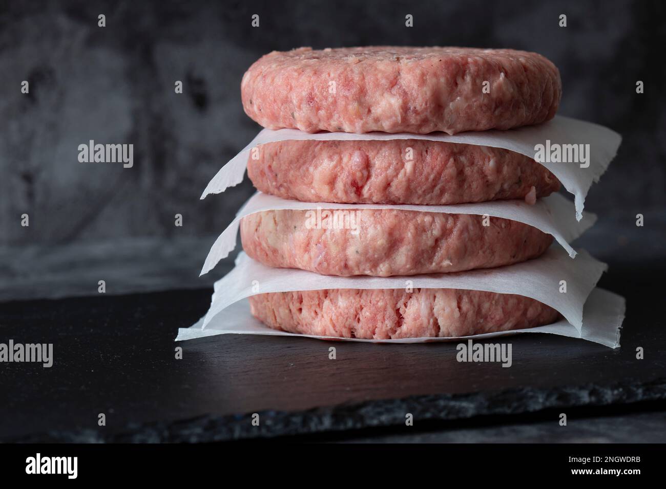 Raw beef burgers stacked on a slate cutting board, separated with ...