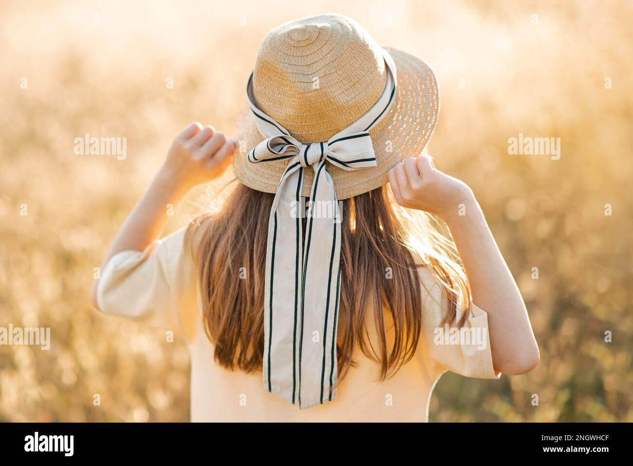 Child girl 5-6 year old wear stylish straw hat laced with ribbon walk in sunny rye meadow ...