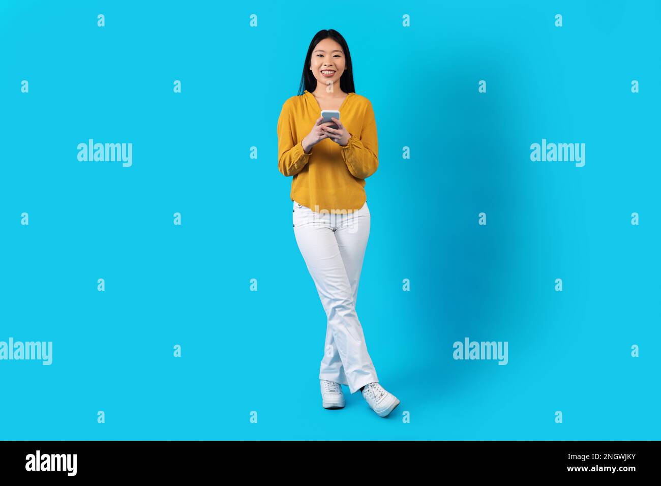 Happy cute japanese woman using cell phone on blue Stock Photo - Alamy