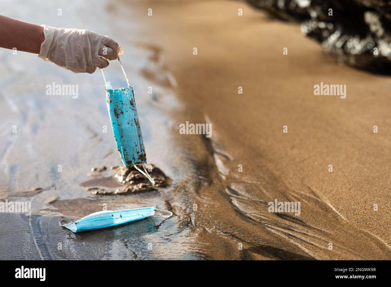 Female hand picking up disposable medical face masks on the beach while ...