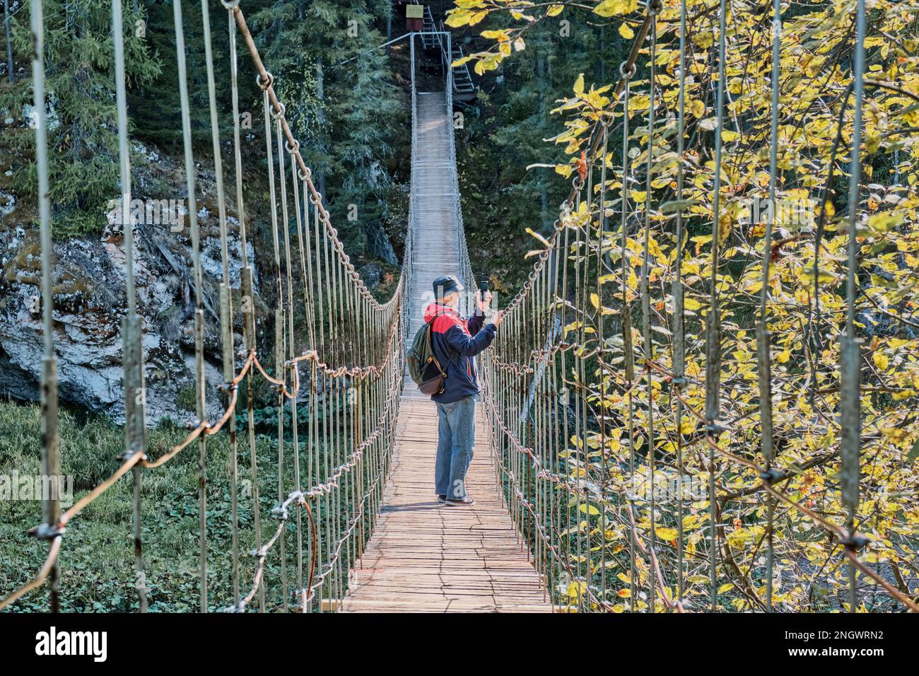 Senior male hiker taking pictures with cell phone on suspension bridge ...