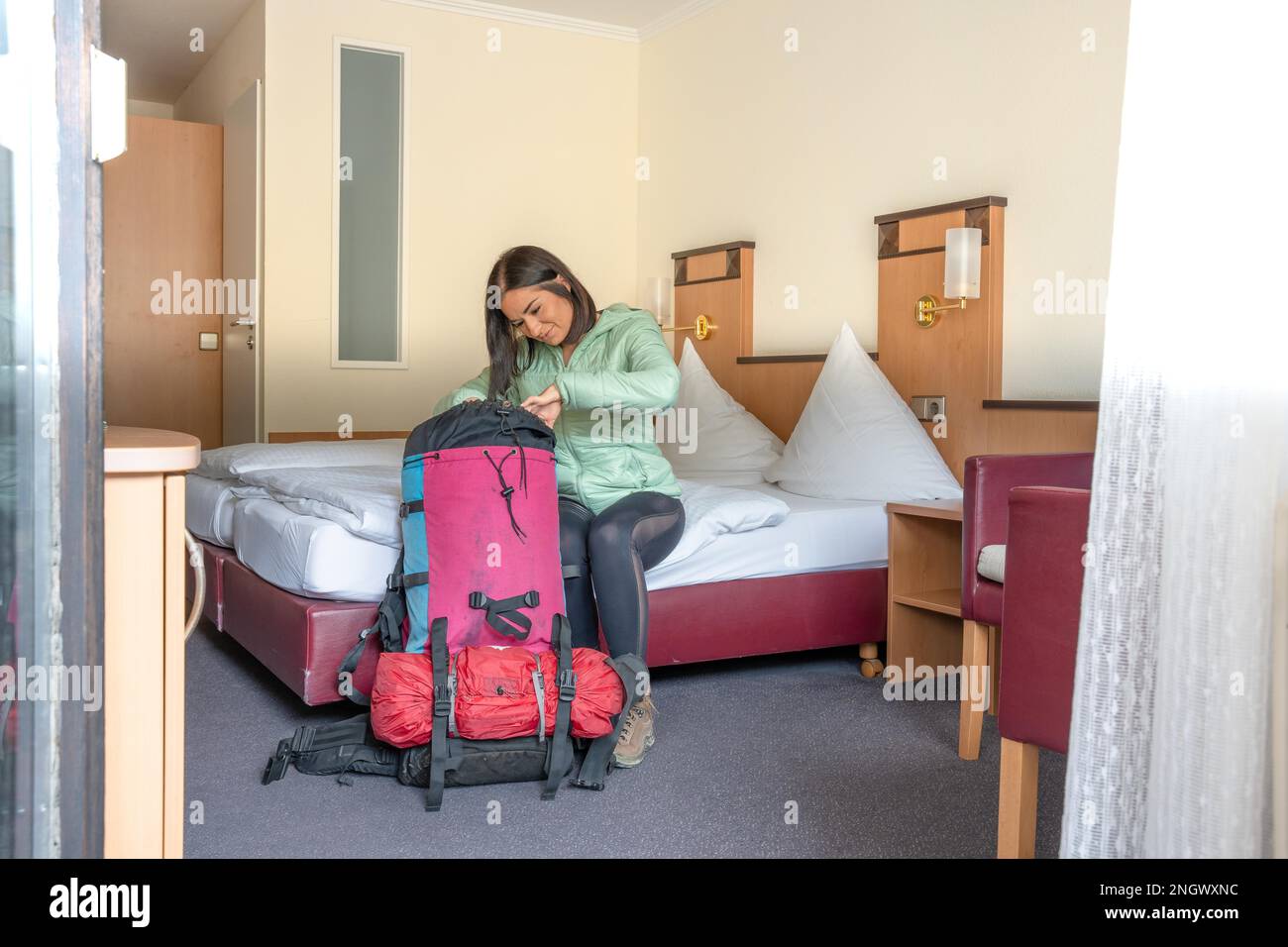 Attractive hiking woman sitting on a hotel bed and looking into her big ...