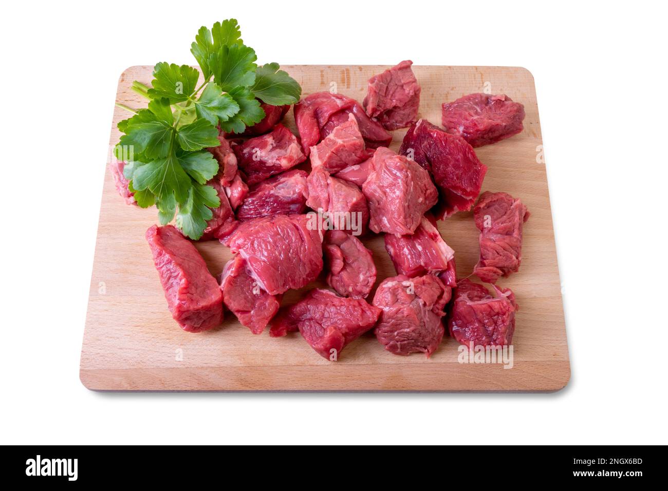 Raw beef diced for stew on wooden cutting board with parsley leaves ...