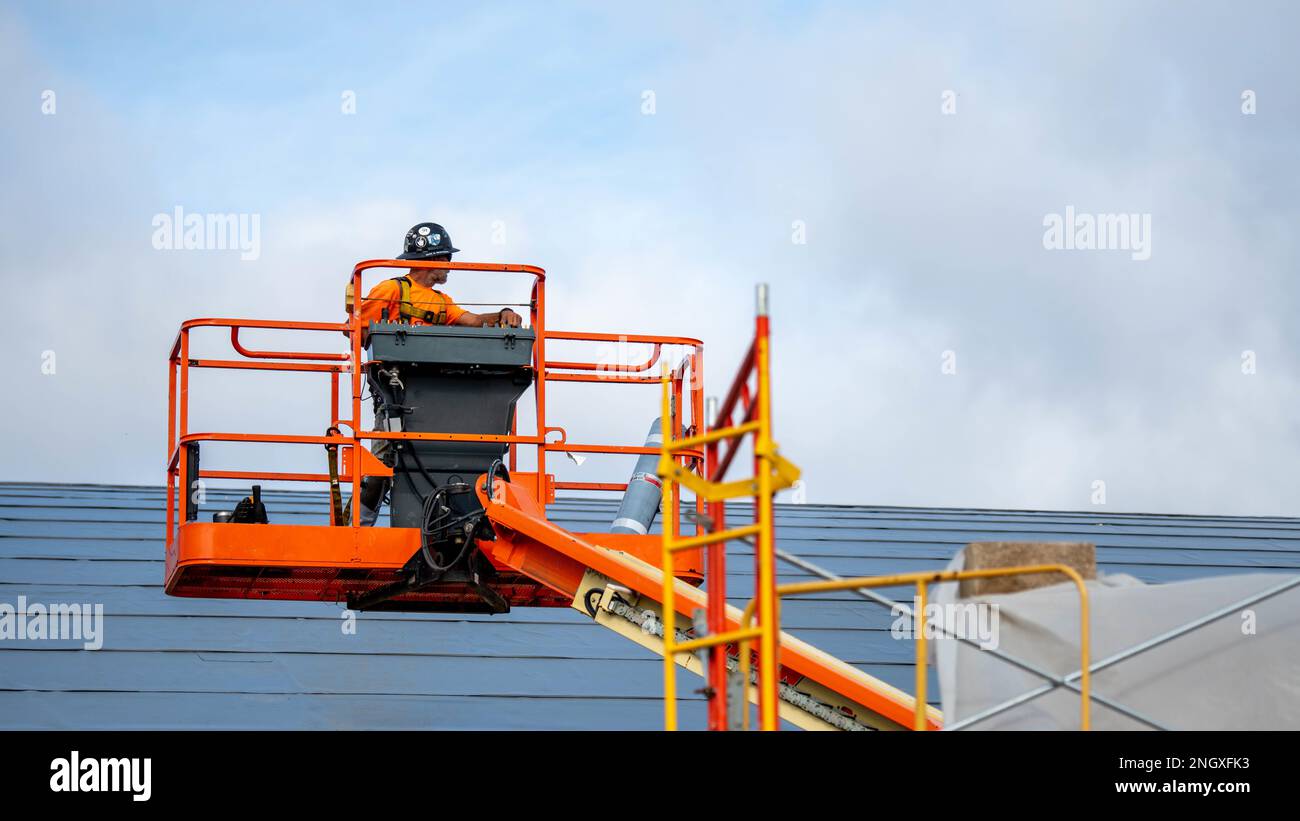 A civilian contractor operates a lift while observing the roof of the ...