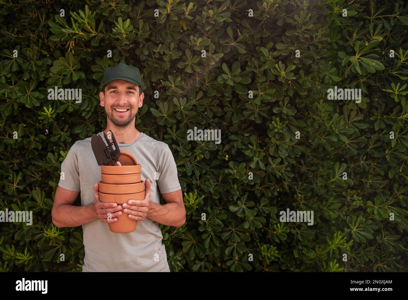 Male gardener in green cap holds terracotta clay pots with gardening ...