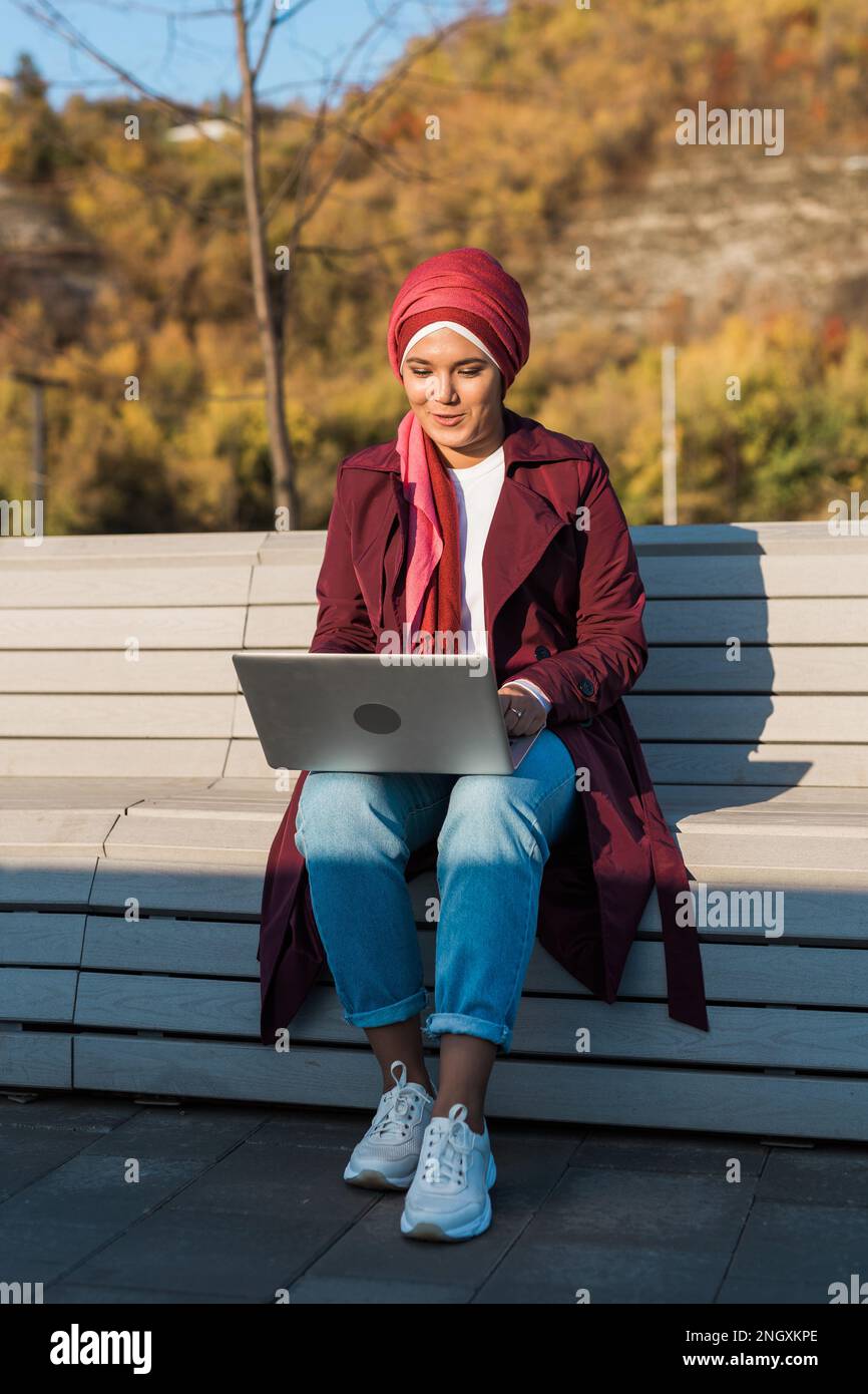 Female muslim arabian student in hijab holding laptop outdoors ...