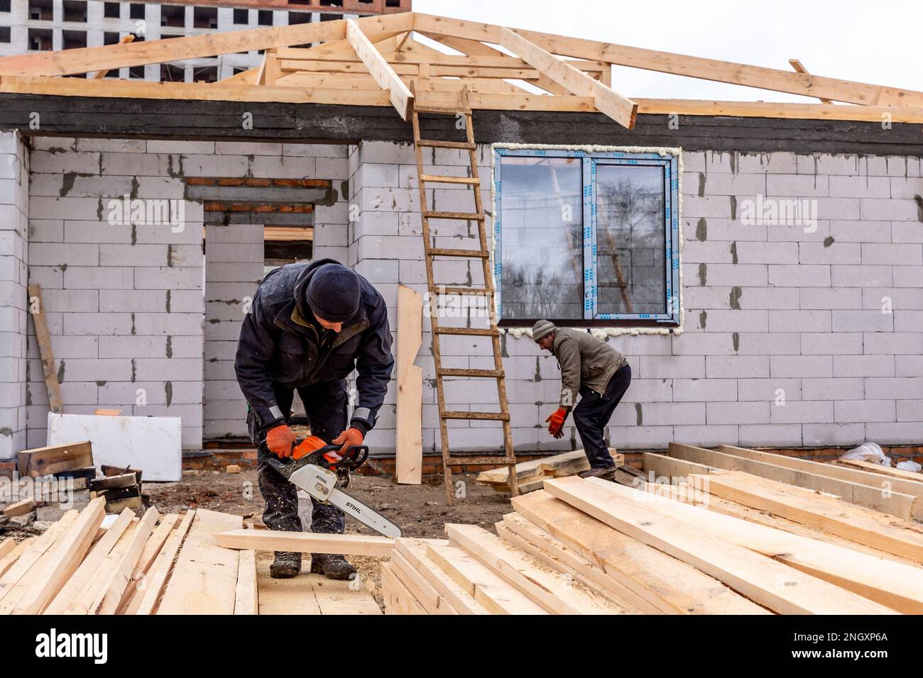 Builders cut wood to build a roof on a new house which replaces a fully ...