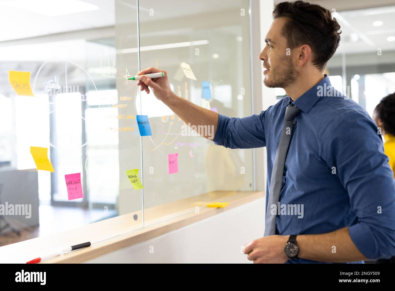 Focused caucasian man working and writing on glass board in office ...